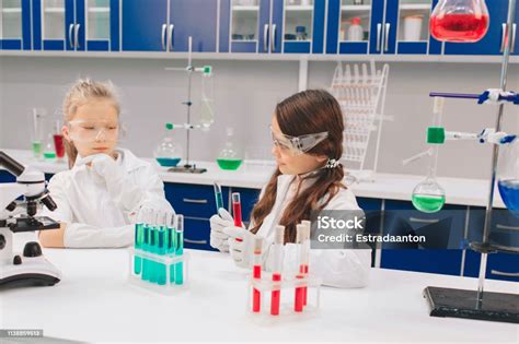 실험실 코트에서 두 작은 아이 학교 실험실에서 화학 학습 실험실 또는 화학 내각에 있는 실험을 만드는 방어적 인 유리에 있는 젊은 과학자 실험에 대 한 재료를 공부 Stem