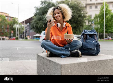 Smiling Woman Using Smart Phone Holding Lunch Box Sitting Cross Legged