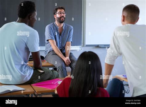 Teacher Involved With Babes At College Sitting On His Desk While Giving An Interactive Class