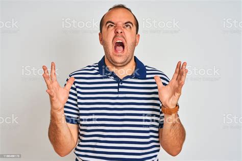 캐주얼 스트라이프 폴로를 입고 고립 된 흰색 배경에 서있는 젊은 남자는 미친 미친 소리와 공격적인 표정과 팔을 들고 고함 좌절