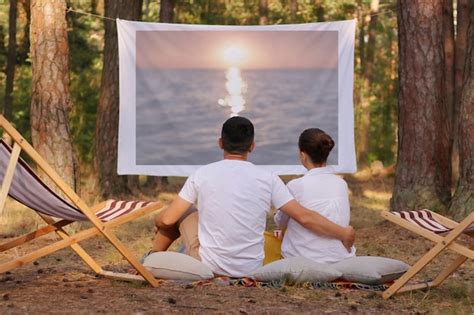 Toma Al Aire Libre De Una Pareja Encantadora Sentada En El Bosque Con Un Proyector Viendo
