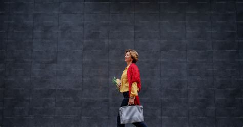 회색 벽을 지나가는 동안 가방과 식료품을 들고 있는 매력적인 백인 패셔너블한 노인 여성의 측면 모습 사진 Unsplash의 한 명의 여성만 이미지