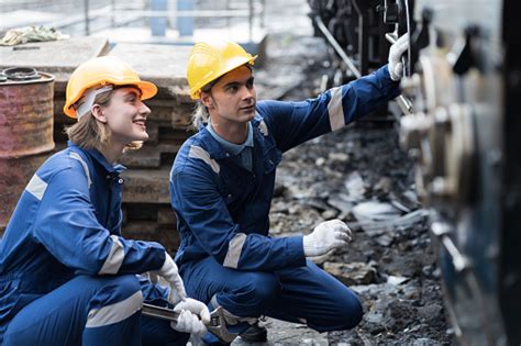 남성과 여성 엔지니어 유지 보수 기관차 엔진 기관차 수리 차고에서 안전 유니폼 헬멧 및 장갑을 착용 남성과 여성 철도 엔지니어는