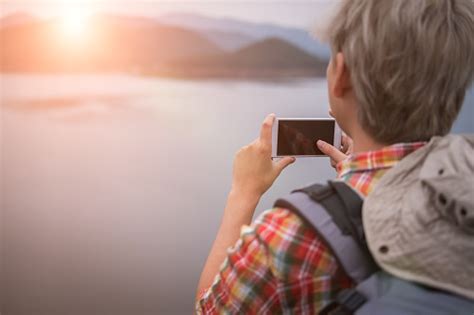 호수 근처 하이킹 배낭 여행자 등산객 남자입니다 백 패 커 관광 스마트 휴대 전화를 사용 하 여 저녁에 사진을 찍어 라이프 스타일 여름 휴가 컨셉 여행 강에 대한 스톡 사진