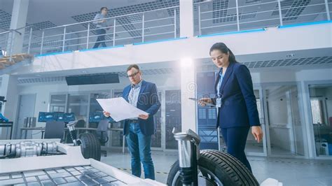 Automotive Design Engineers Looking At Technical Drawings Of A Electric