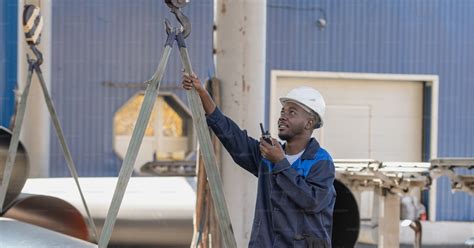 작업복과 안전모를 쓴 아프리카 민족의 젊은 공장 노동자가 워키토키를 사용하면서 작업 중 큰 파이프를 들어 올리는 것을 통제합니다 사진 Unsplash의 보호 작업복 이미지