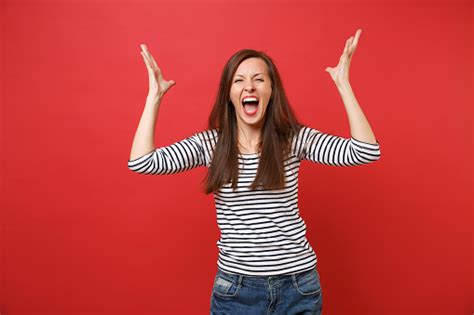 캐주얼 스트라이프 옷 비명 상승 하 고 밝은 빨간 벽 배경에 고립 손 확산에 미친 젊은 여자의 초상화 사람들이 진심으 감정 라이프 스타일 개념 복사 공간을 비웃는 다 갈색