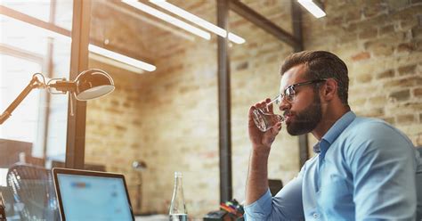 휴식이 필요해 안경을 쓰고 정장을 입은 목마른 수염 사업가는 현대적인 사무실에서 일하는 동안 신선한 물을 마시고 있습니다 사업 개념입니다 작업 개념 사진