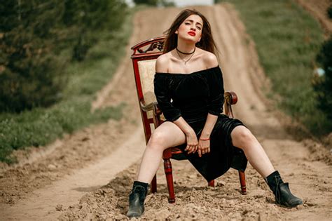 검은 드레스에 아름 다운 젊은 여자는 모래도로에 고전적인 안락의 자에 앉아 사진 작가를 위한 포즈 건강한 생활방식에 대한 스톡 사진 및 기타 이미지 Istock