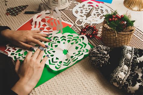 소녀는 크리스마스 나 새해를 축하하기 위해 종이에서 눈송이를 잘라 흰색과 색종이 가위 마커 화이트 레이스 식탁보에 계절 장식