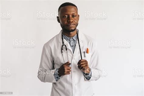 흰색 배경에 흰색 유니폼을 입고 서있는 젊은 아프리카 계 미국인 의사의 클로즈업 사진 건강관리와 의술에 대한 스톡 사진 및 기타 이미지 건강관리와 의술 격리 구급대원