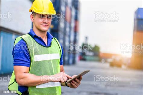 디지털 태블릿을 사용하고 노란색 안전 헬멧을 착용하고 수입 및 수출 운송을 위해화물 화물 선에서 컨테이너 상자를 제어 할 수 있는지 확인하는 젊은 자신감 백인 남자 엔지니어