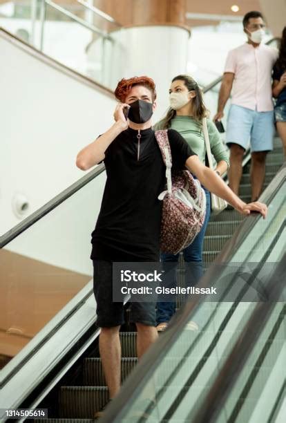쇼핑몰 에스컬레이터에서 휴대 전화로 말하는 얼굴 마스크를 쓴 남자 코로나바이러스에 대한 스톡 사진 및 기타 이미지 코로나바이러스 사진 이미지 세로 구도 Istock