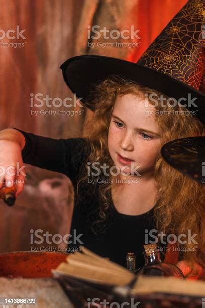 검은 마녀 의상과 모자를 쓴 귀여운 붉은 머리 소녀가 책을 읽고 할로윈 장식으로 요술 물약을 만듭니다 할로윈 개념 마녀에 대한 스톡 사진 및 기타 이미지 Istock