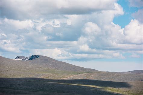 회색 바위가 많은 산맥이있는 미니멀리스트 산맥과 눈 꼭대기에는 햇빛과 변화하는 날씨에 구름의 그림자가 있습니다 햇볕이 잘 드는 바위 산과 흐린 하늘이있는 최소한의 고산 풍경