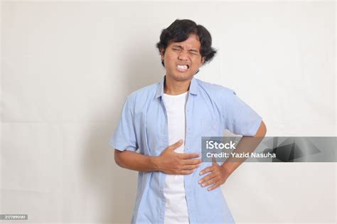 파란 셔츠를 입은 지친 아시아 남자의 초상화는 배에 통증을 느끼고 배고픔을 참습니다 배가 아프고 배고픈 음식 개념 흰색 배경에 고립된 이미지 20 24세에 대한 스톡 사진