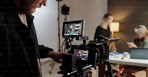 비디오 카메라를 든 젊은 남자가 문서를 들고 어시스턴트 앞에 서서 상업 촬영에 참여하는 여성 모델 사진 Unsplash의 사진술 이미지