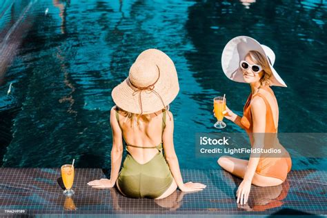 오렌지 칵테일과 함께 풀 사이드에 앉아 수영복과 모자를 핀 업 하는 여자의 뒷 전망 2명에 대한 스톡 사진 및 기타 이미지 2명 금발 머리 물 Istock