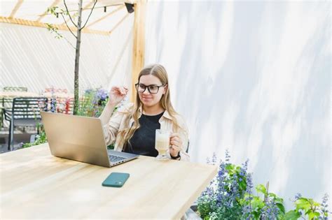 Premium Photo Cute European Woman Sitting At Outdoor Cafe Table With Laptop And Cup Of Coffee