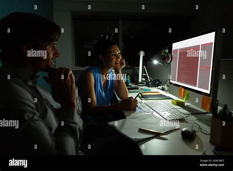Two Diverse Male And Female Colleagues Sitting At Desk And Using Computer With Coding On Screen
