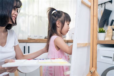 아시아 의 젊은 행복한 아이 딸 어머니와 함께 그림 보드에 착색 행복한 가족 활동 어린 소녀 아이는 수채화 페인트와 브러시와 함께 예술 사진을 그리는 방법을 배우고 엄마와