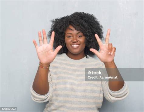 젊은 아프리카계 미국인 플러스 크기 여자 및 손가락으로 가리키는 스웨터를 입고 회색 그런 지 벽에 번호 8 자신감과 행복 미소 동안 8에 대한 스톡 사진 및 기타 이미지