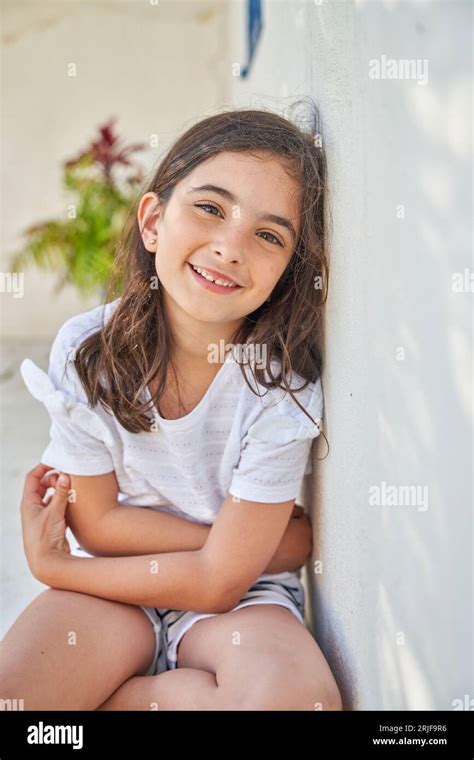 Adorable Cheerful Preteen Girl In T Shirt And Shorts Sitting On Street With Crossed Arms And