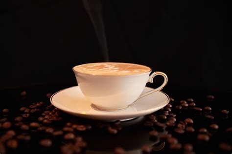 검은 표면에 뜨거운 커피 한 잔을 클로즈업합니다 검은 표면에 카푸치노와 커피 콩 한 잔 라떼 아트가 있는 이탈리아 커피 검정색