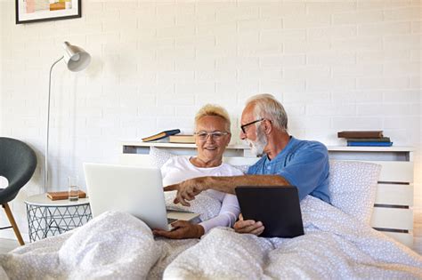 디지털 태블릿과 노트북을 사용하여 침대에서 미소 짓는 선임 커플 2명에 대한 스톡 사진 및 기타 이미지 2명 가정 생활 기혼 Istock