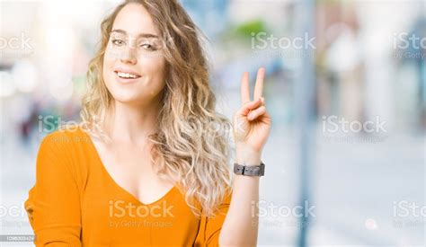 승리 표시를 하 고 카메라에 윙크 하는 행복 한 얼굴로 웃 고 고립 된 배경 위에 아름 다운 젊은 금발 여자 번호 2입니다 곱슬 머리에 대한 스톡 사진 및 기타 이미지