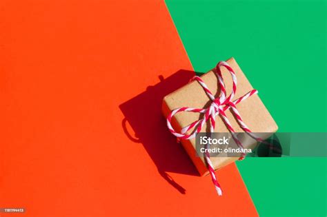 듀오톤 레드 그린 배경 하드 그림자 가혹한 빛에 줄무늬 꼬기와 함께 묶여 갈색 크래프트 종이에 싸여 선물 상자 트렌디 한 크리스마스 새해 카드 포스터 휴일 선물 쇼핑 개념
