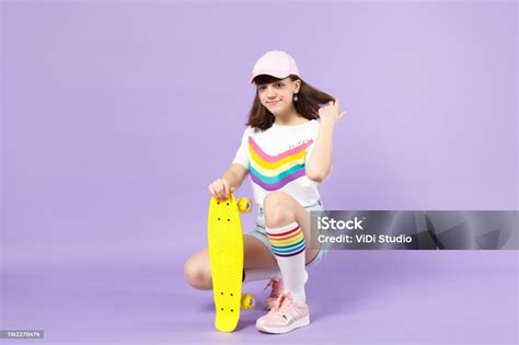 생생한 옷에 아름 다운 십 대 소녀 앉아 노란색 스케이트 보드 스튜디오에서 보라색 파스텔 벽 배경에 고립 된 찾고 카메라 사람들은 진심으로 감정 라이프 스타일 개념입니다