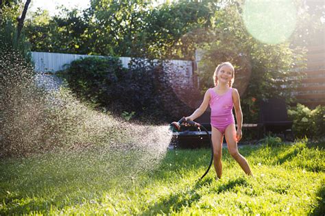 정원 호스를 가지고 놀고 햇볕이 잘 드는 뒤뜰에서 물 스프레이로 즐거운 시간을 보내는 행복한 어린이 소녀 서머 타임 꼬마 소녀는 호스로 정원에 물을 주는 것을 돕습니다 작은