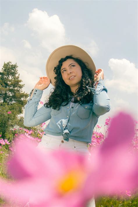 검은 상단 경치 고위 여성 꽃 꽃무늬 나라 장면 노란 꽃 노란 꽃잎 노인 노인 여성 녹색 줄기 농촌의 들판 만족 멀리보고 모자 미소 짓는 밝은