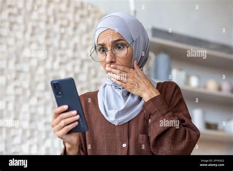 Junge araberin im Hijab zu Hause in der Küche schockiert auf ein Telefon schaut Sie hielt