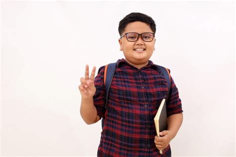 Счастливый азиатский школьник стоит показывая два пальца на белом фоне