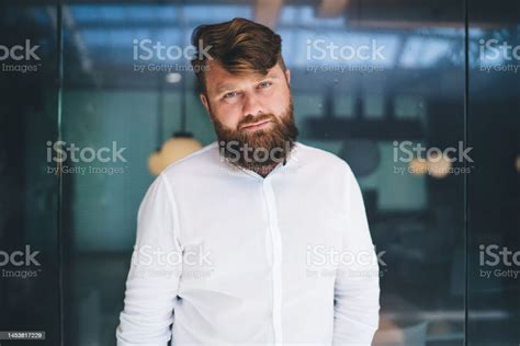 브랜드 이름을 위한 복사 공간이 있는 흰색 스마트 캐주얼 셔츠를 입은 남성적인 수염 난 사업가의 절반 길이 초상화 현대적인 작업 공간에서 포즈를 취하는 자신감 넘치는 백인