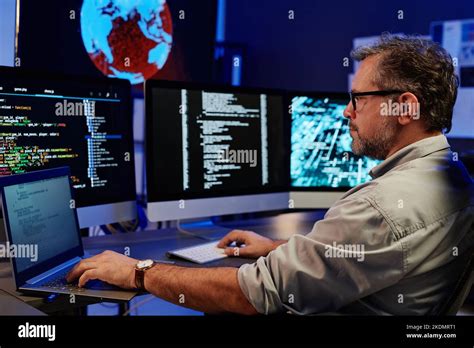 Side View Of Serious Server Engineer Using Laptop And Computers While