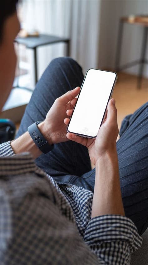 Partially Visible Person Holds Smartphone Seated On Couch With Checkered Shirt And Dark