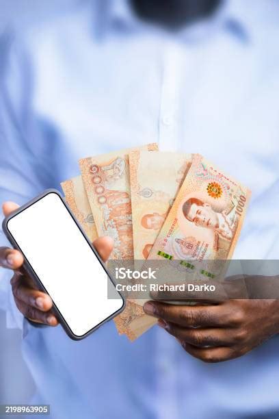 태국 바트 지폐를 들고 빈 화면이 있는 전화기를 카메라에 보여주는 흑인 미국 지폐를 들고 있는 손 3d 렌더링 된 돈 가나에 대한 스톡 사진 및 기타 이미지 Istock