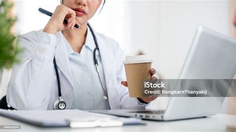 전문적이고 사려 깊은 동양인 여성 의사가 병원 사무실의 책상에서 일하고 있습니다 25 29세에 대한 스톡 사진 및 기타 이미지 25 29세 건강관리와 의술 결정
