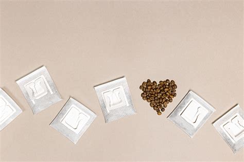 커피 원두에서 커피 백과 심장을 떨어 뜨리고 컵에서 양조하기위한 분쇄 커피 종이 봉지 드립 커피 필터 베이지 색 배경 상단보기 카피 스페이스가있는 최소 플랫 레이 팩