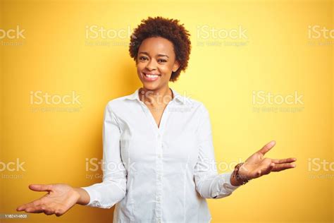 고립 된 노란색 배경을 통해 아프리카 계 미국인 비즈니스 여성은 친절한 환영 긍정적이고 자신감있는 인사로 두 팔을 벌려 쾌활한 미소를 지었습니다 길이에 대한 스톡 사진 및