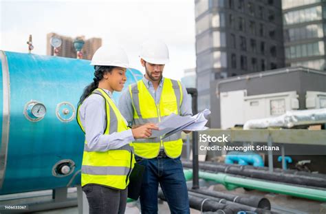 몇 명의 전문 엔지니어 또는 기술자 근로자가 건설 현장의 파란색 인쇄물로 토론하고 건물 갑판의 탱크 근처에 머물러 있습니다 25 29세에 대한 스톡 사진 및 기타 이미지