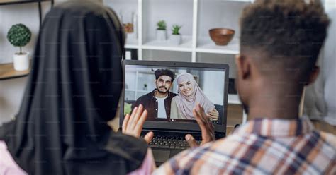 히잡을 쓴 아프리카계 미국인 남성과 무슬림 여성이 노트북으로 친척들과 화상 회의를 하면서 손을 흔들고 있다 전염병 기술 및 통신의 개념 사진 Unsplash의