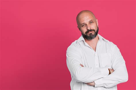 분홍색 배경 앞에서 포즈를 취하는 접힌 팔과 데드팬 표정을 가진 진지한 중년 남성 40 49세에 대한 스톡 사진 및 기타 이미지