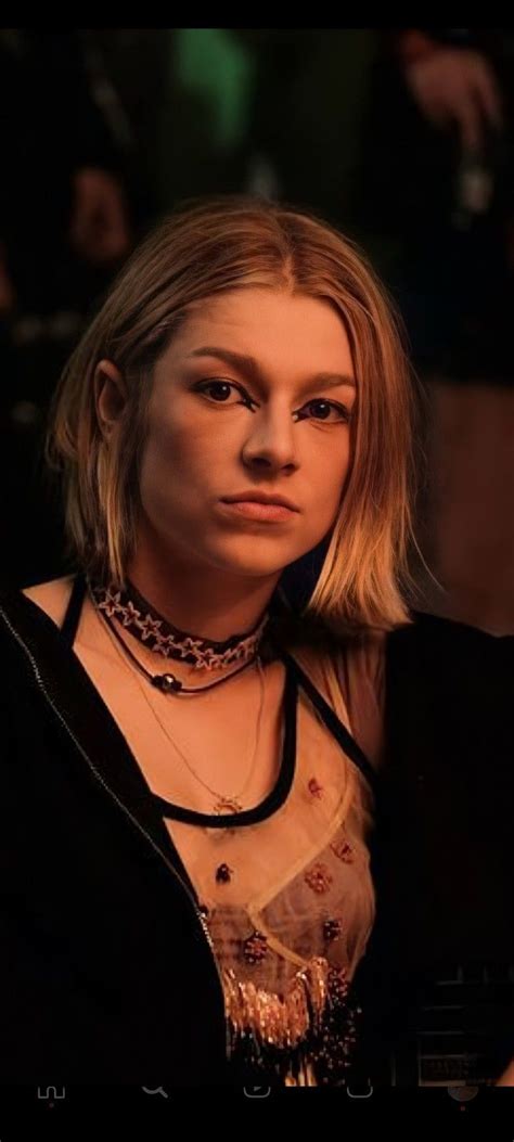 A Woman With Blonde Hair Wearing A Black Jacket And Gold Necklace Is Looking At The Camera