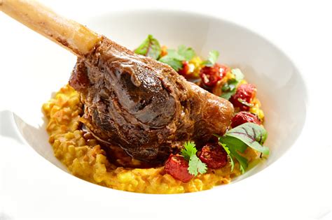 호박 스튜와 구운 토마토를 곁들인 양고기의 느린 구운 다리 흰색 배경에 고립 된 야채가있는 양고기 다리 훌륭한 식사에 대한 메인 코스 뼈에 고기에서 미식가 요리 고기 메뉴