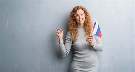 매우 행복 한 측에 손 및 손가락으로 가리키는 러시아의 국기를 들고 회색 그런 지 벽에 빨강 머리 젊은 여자 가리키기에 대한 스톡 사진 및 기타 이미지 Istock