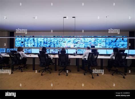 Group Of Security Data Center Operators Working In A CCTV Monitoring Room Looking On Multiple